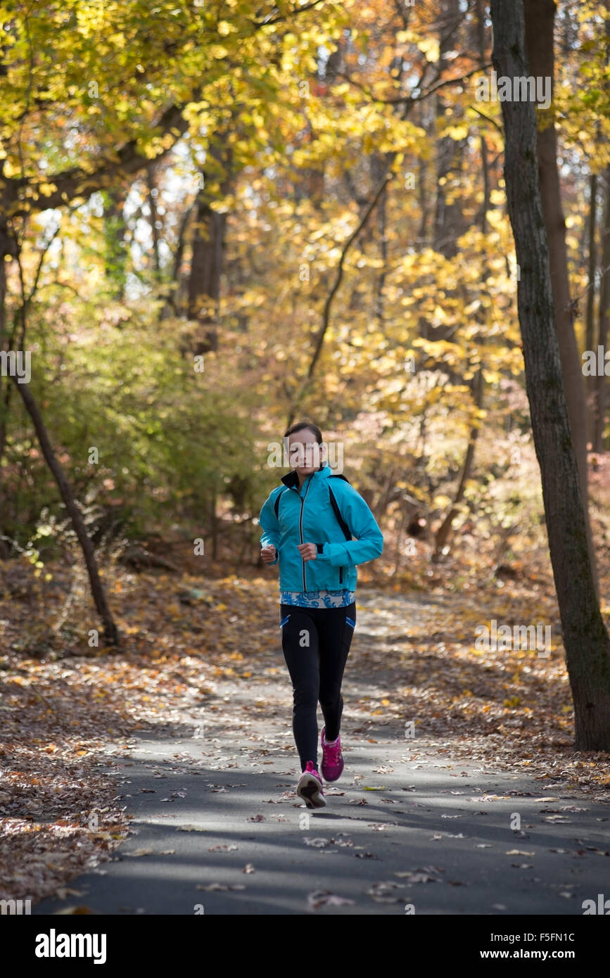 Teenage girl running alone on a forested path on a bright Fall day in ...