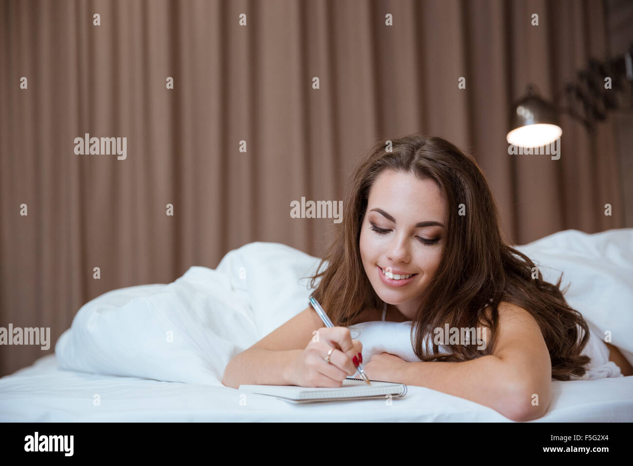 Portrait of a young happy woman making notes in notepad while lying on ...