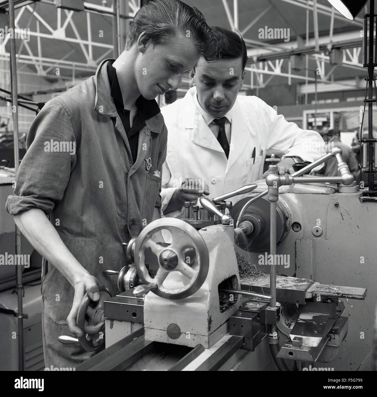 1950s historical, a young male apprentice using an industrial metal ...