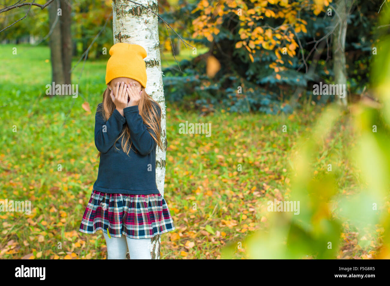 Little girl playing hide and seek near tree in autumn park Stock Photo ...