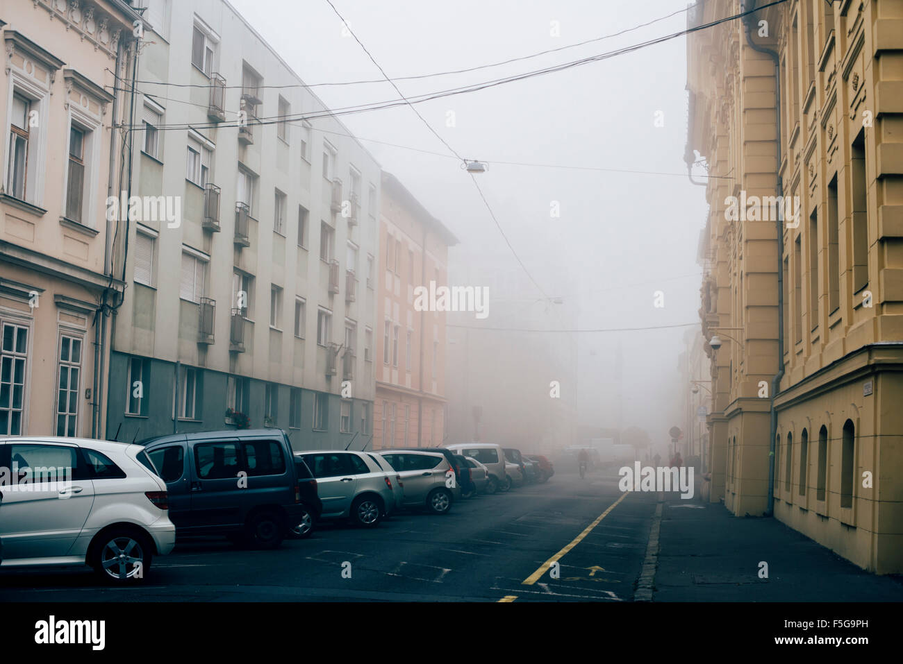 Empty street with cars parks left side of asphalt road on misty autumn ...