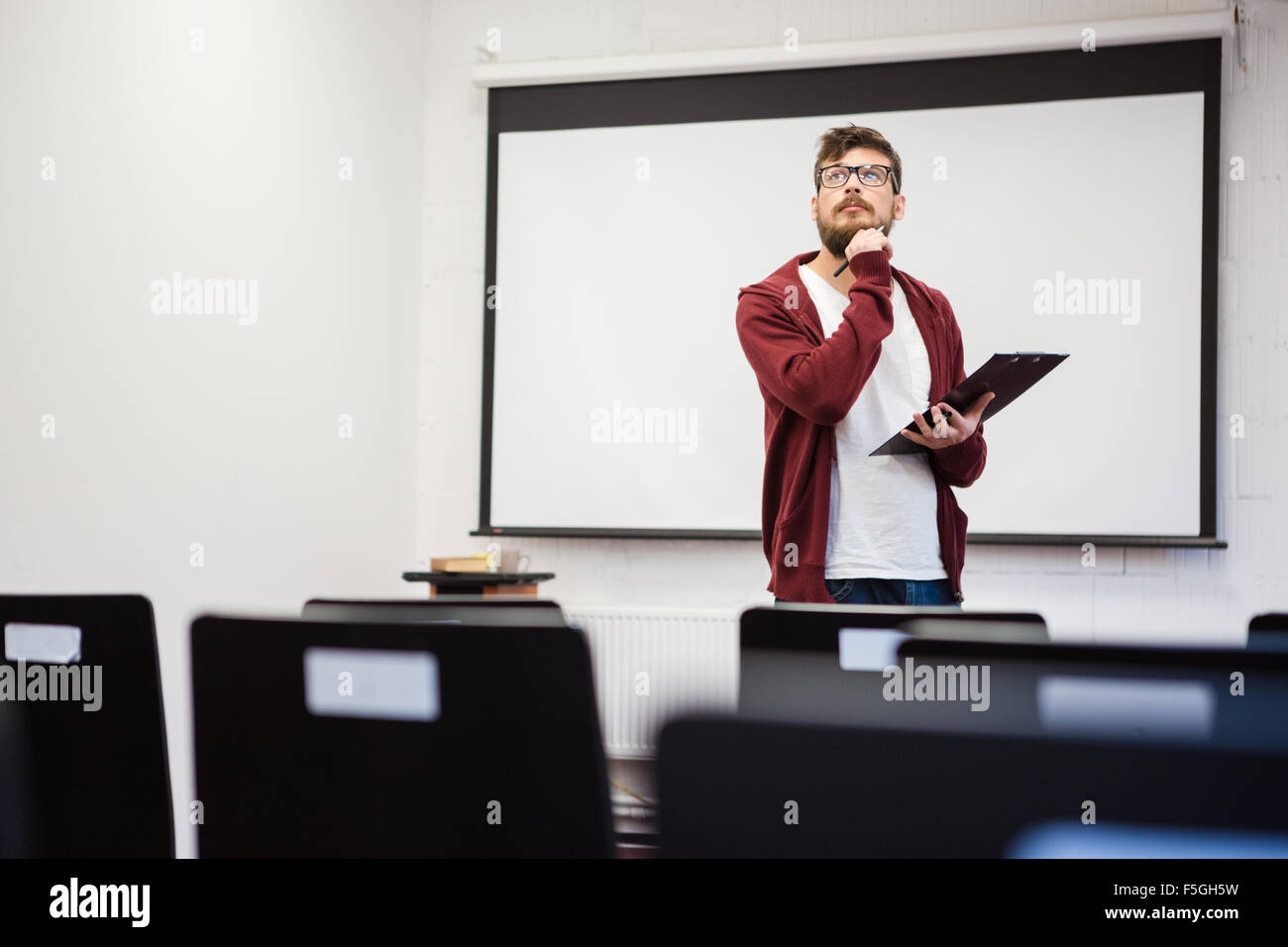 Young modern teacher with beard preparing for the lecture in classroom ...