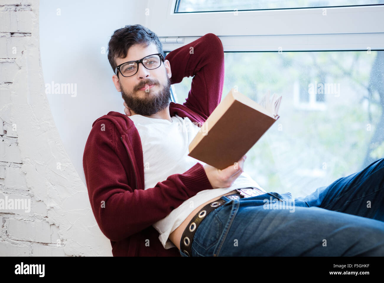 Student with beard in glasses sitting on window sill and reading Stock ...