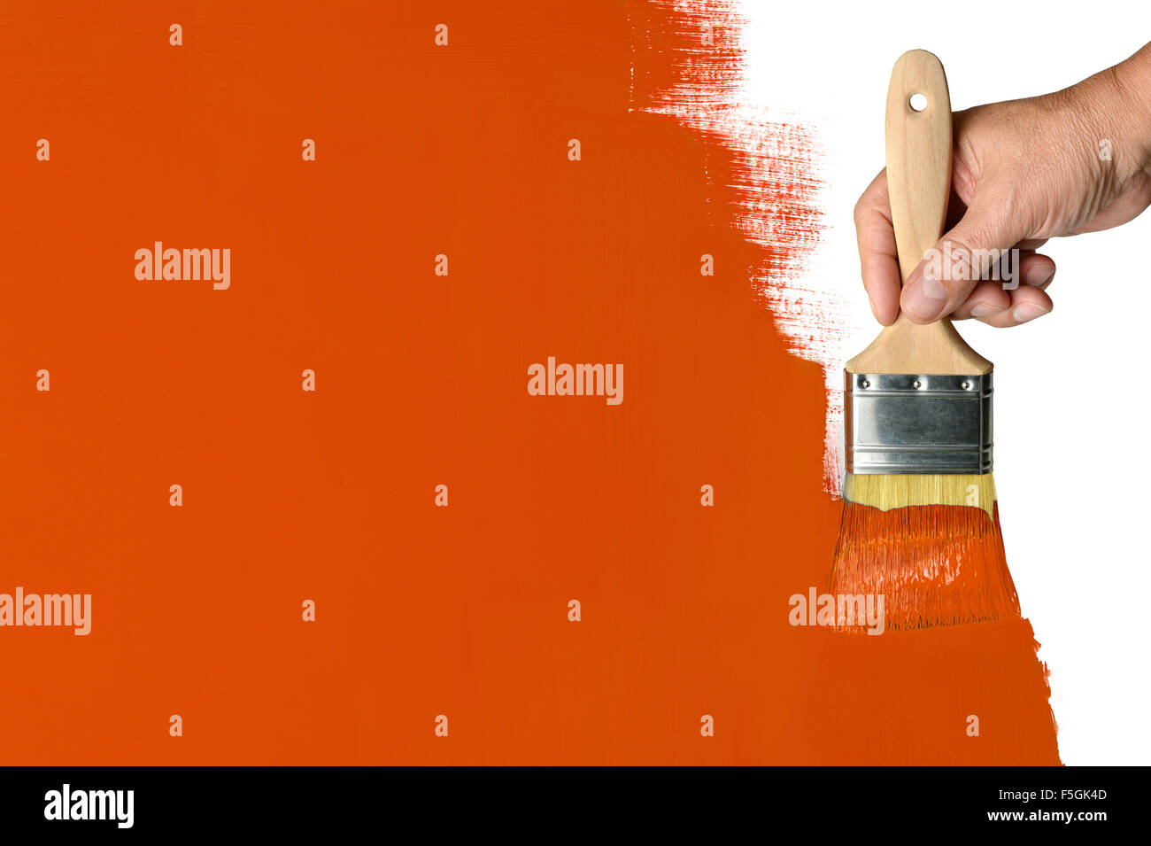 Man's hand using paintbrush with orange paint on wall Stock Photo - Alamy
