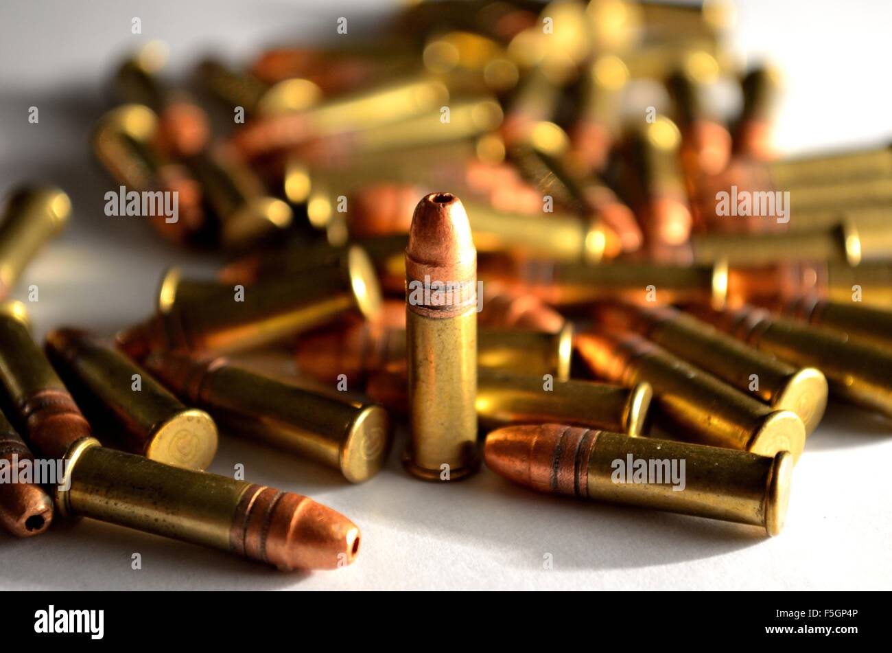 single standing bullet amongst other in a pile on white background ...