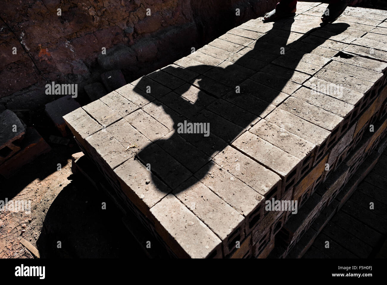A shadow of a working child is seen on a pile of bricks at a brick ...