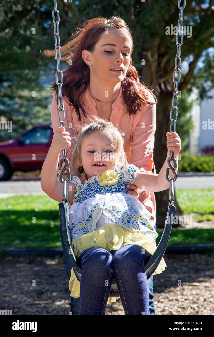 Beautiful mother pushing cute young daughter on swings, town park Stock ...