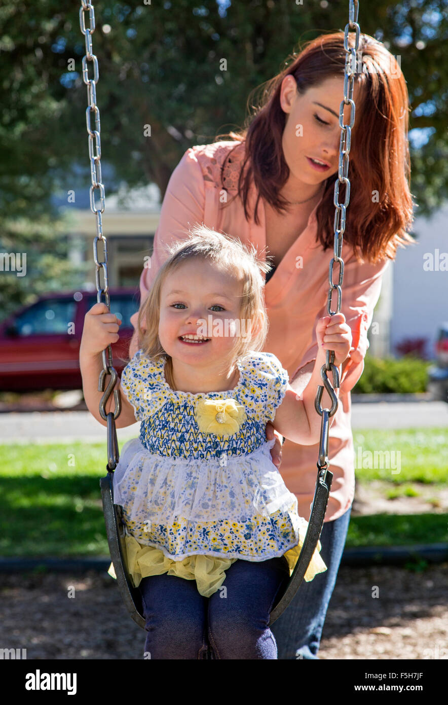 Beautiful mother pushing cute young daughter on swings, town park Stock ...
