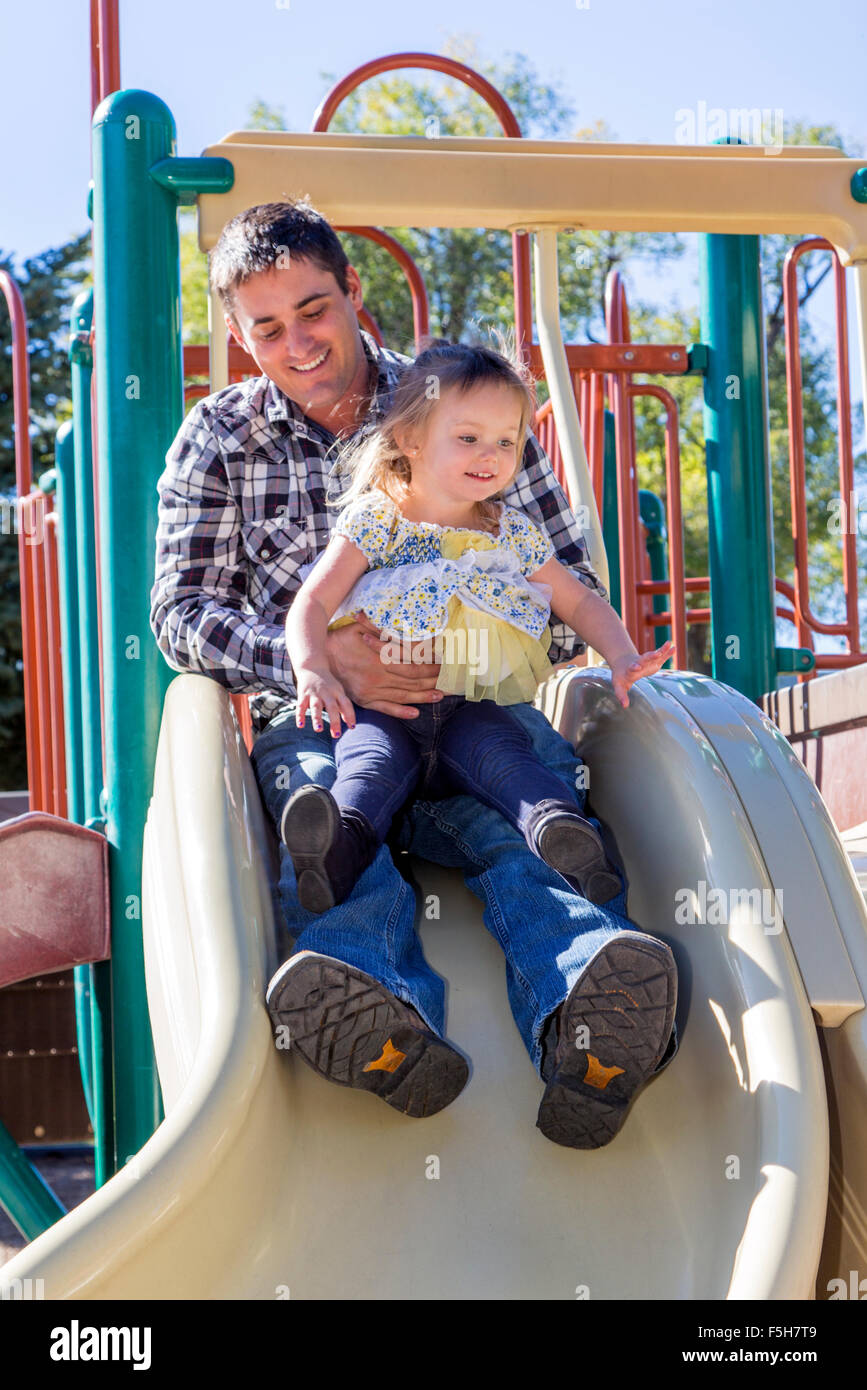 Father and young daughter playing on a sliding board, park playground ...
