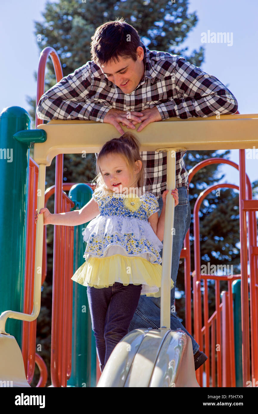 Father and young daughter playing on a sliding board, park playground ...