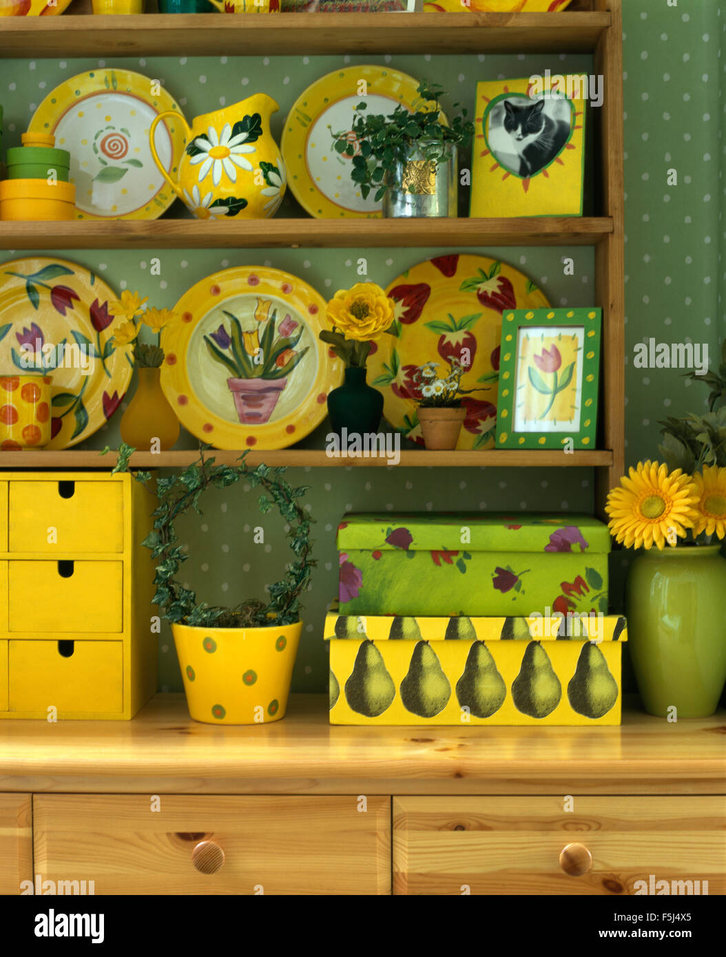 Bright yellow and green crockery and storage boxes on pine shelves in a ...