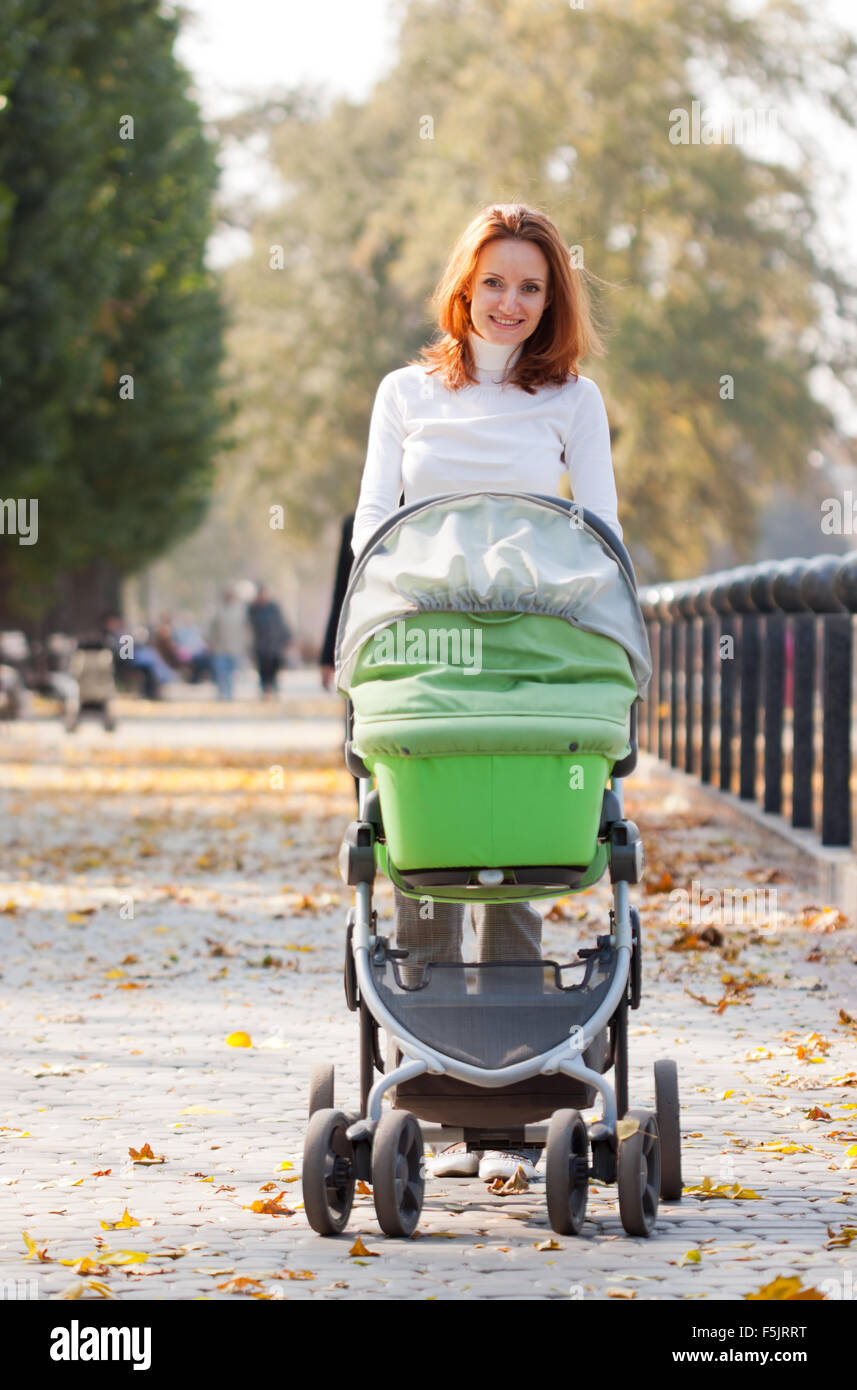 Happy young mother with baby in buggy walking in autumn park Stock ...