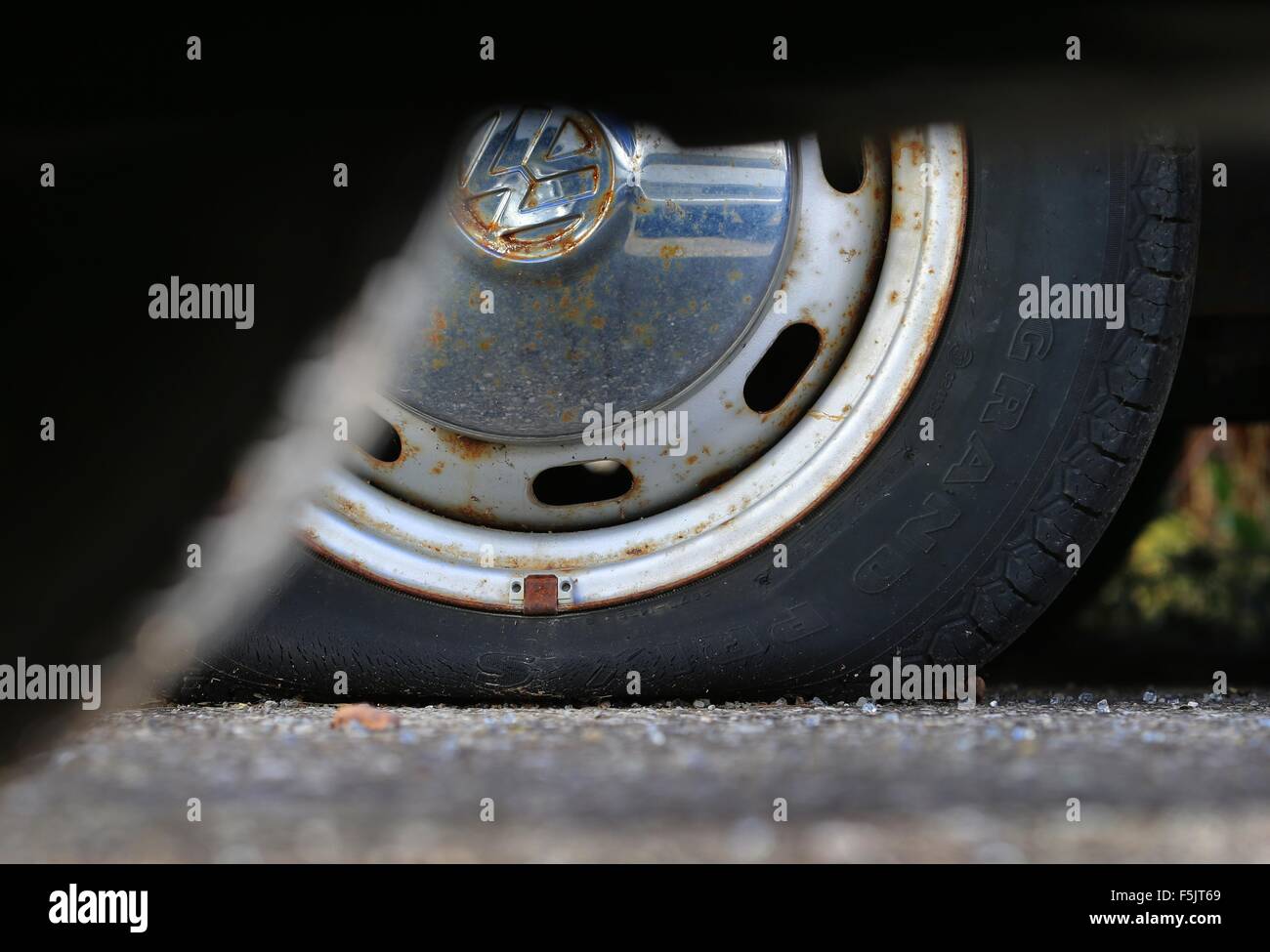 A rusty VW Logo on an old VW Beetle with a flat tire at a garage in ...