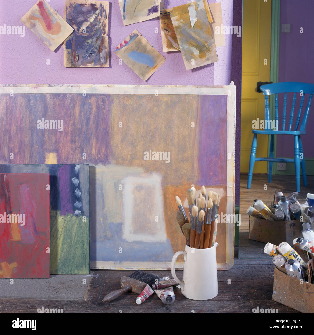 Paintbrushes in jug on floor against an abstract painting in an artist ...