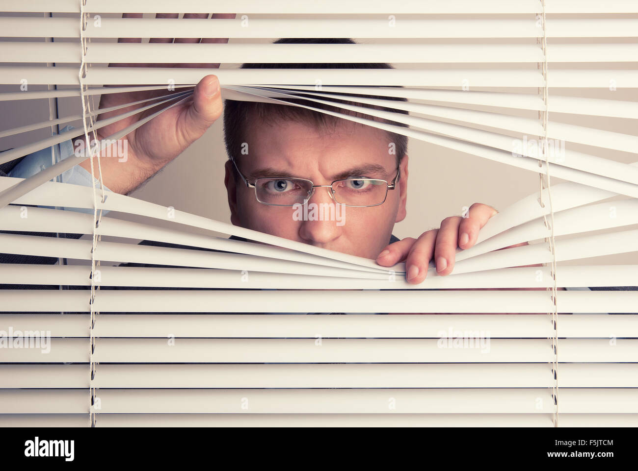 A young man looking through window blinds Stock Photo - Alamy