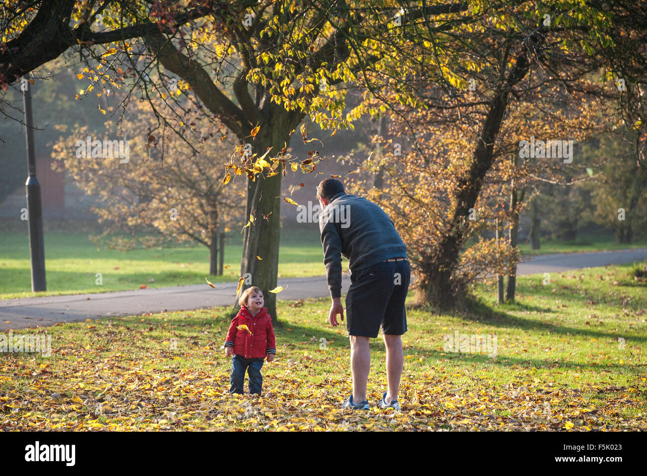 A man throws fallen leaves in the air for his child in a London park ...