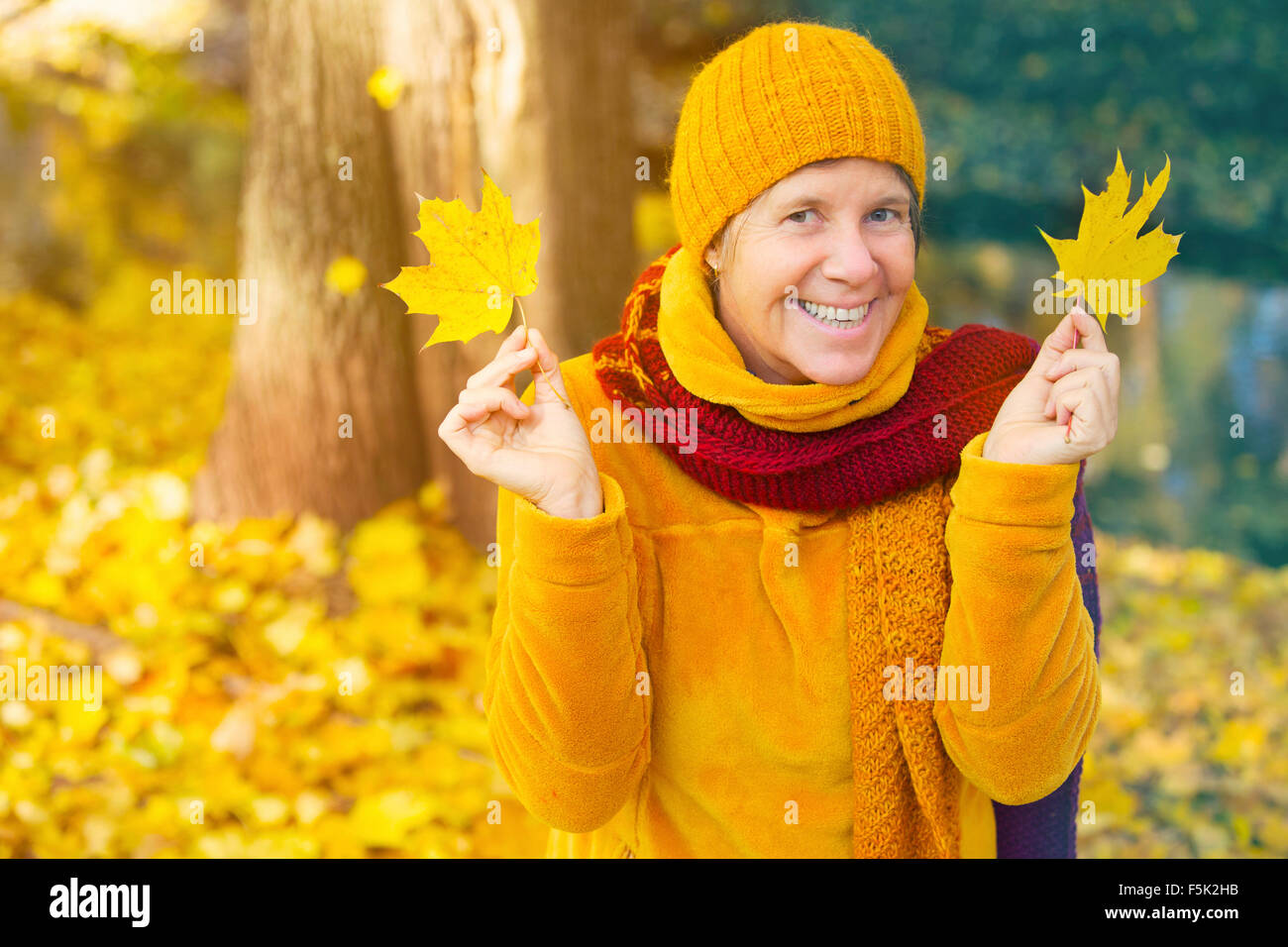 woman standing in front of trees in the fall and holding leaves in her ...