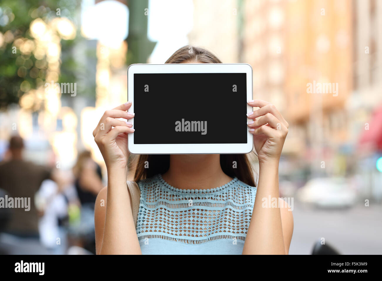 Woman covering her face with a blank tablet screen showing display ...