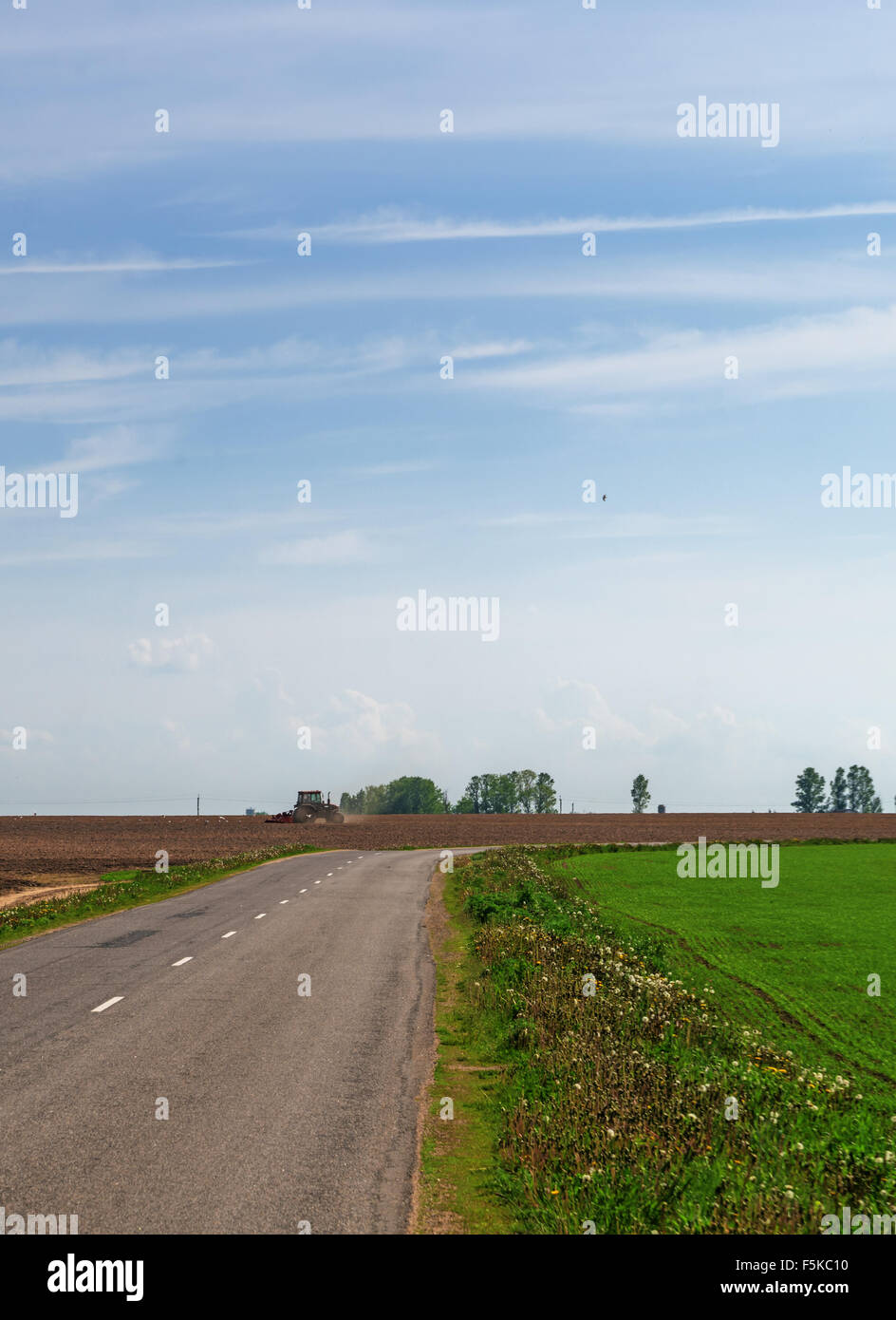 Asphalt road through field with tractor Stock Photo - Alamy