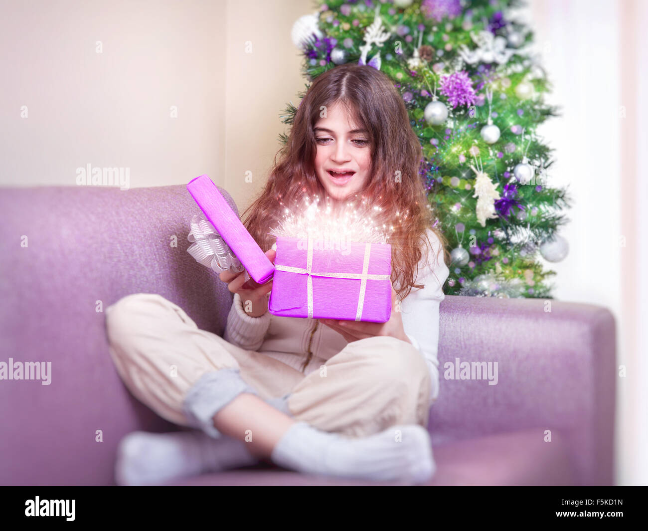 Cheerful teen girl opening gift box with magic glowing present, sitting ...
