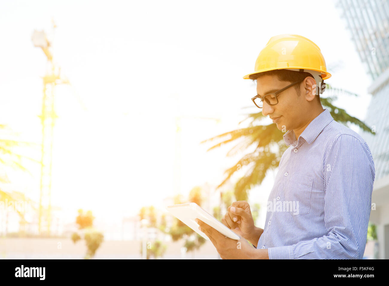 Asian Indian male contractor engineer with hard hat hand holding tablet ...