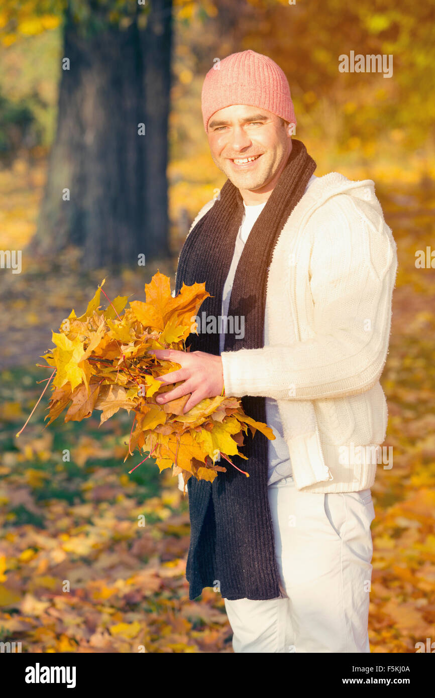 man standing next to trees in fall and holding leaves in his hands ...