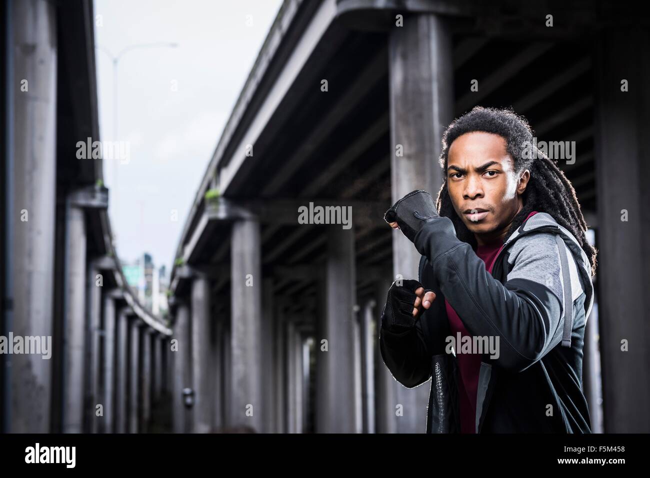 Portrait of male boxer with fists raised standing below urban flyover ...