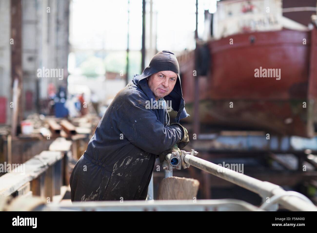 Portrait of worker leaning against railings in shipyard workshop Stock ...