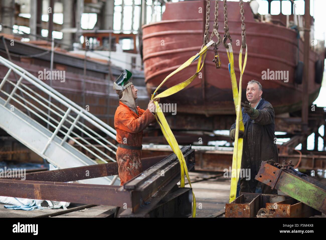 Workers using winch for girders in shipyard workshop Stock Photo - Alamy