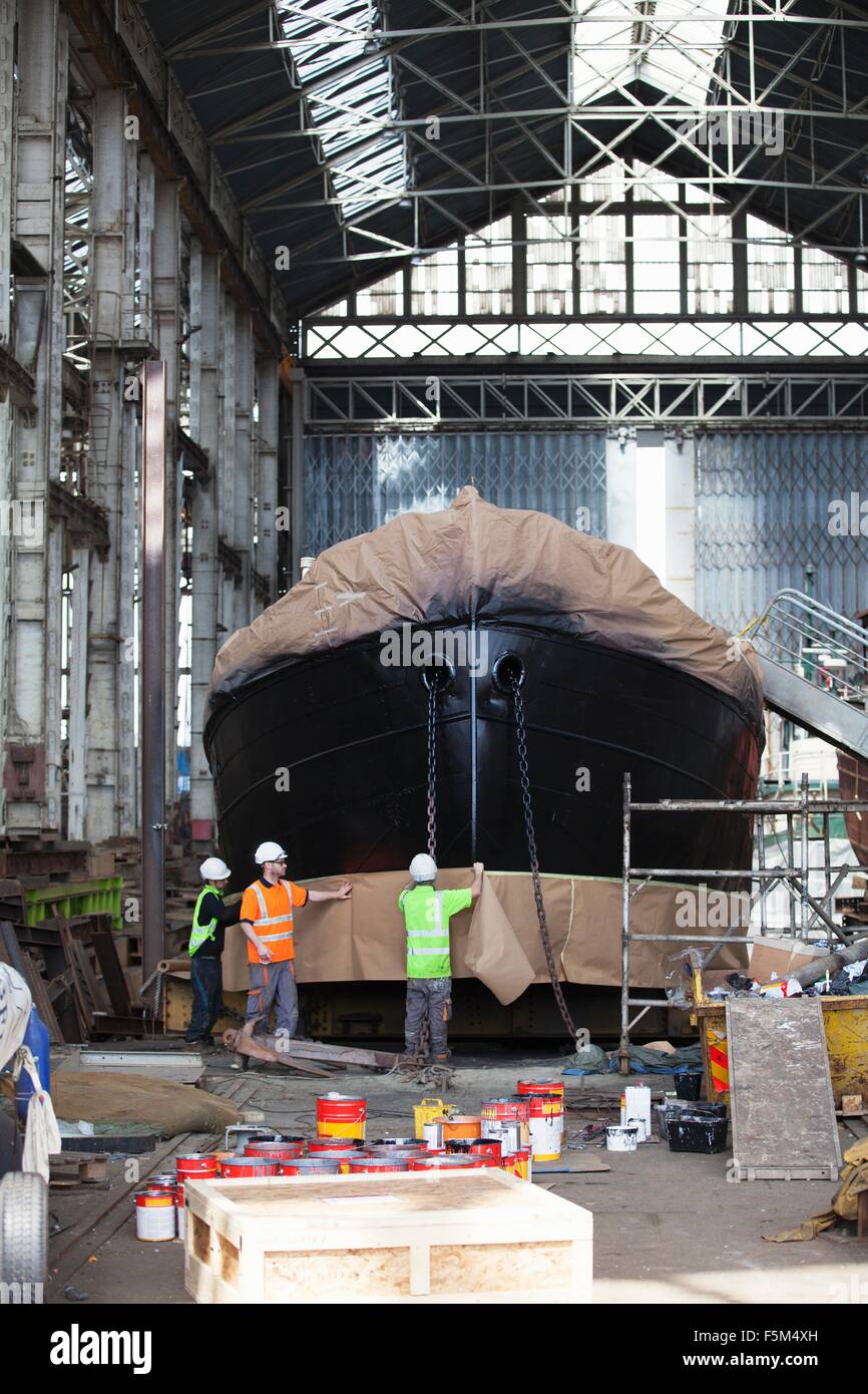 Three workers wrapping boat in shipyard Stock Photo - Alamy