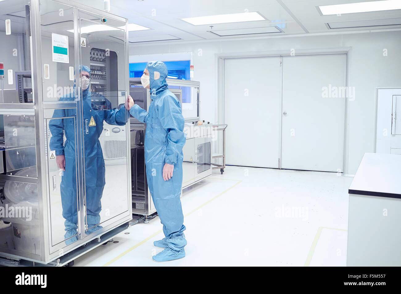 Male worker inspecting manufacturing machinery in flexible electronics ...