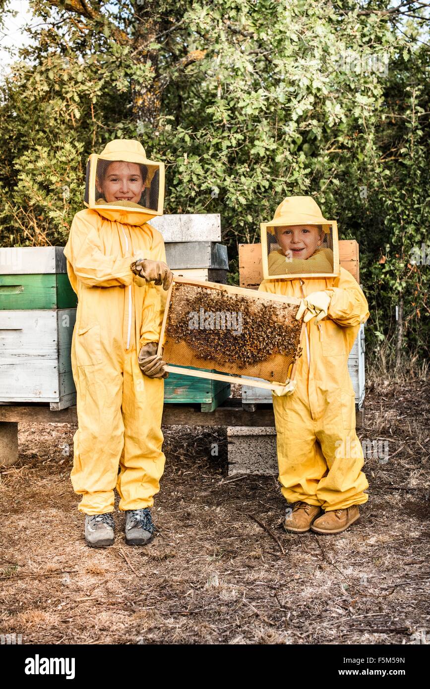 Portrait of young girl and boy in beekeeper dress holding hive frame ...