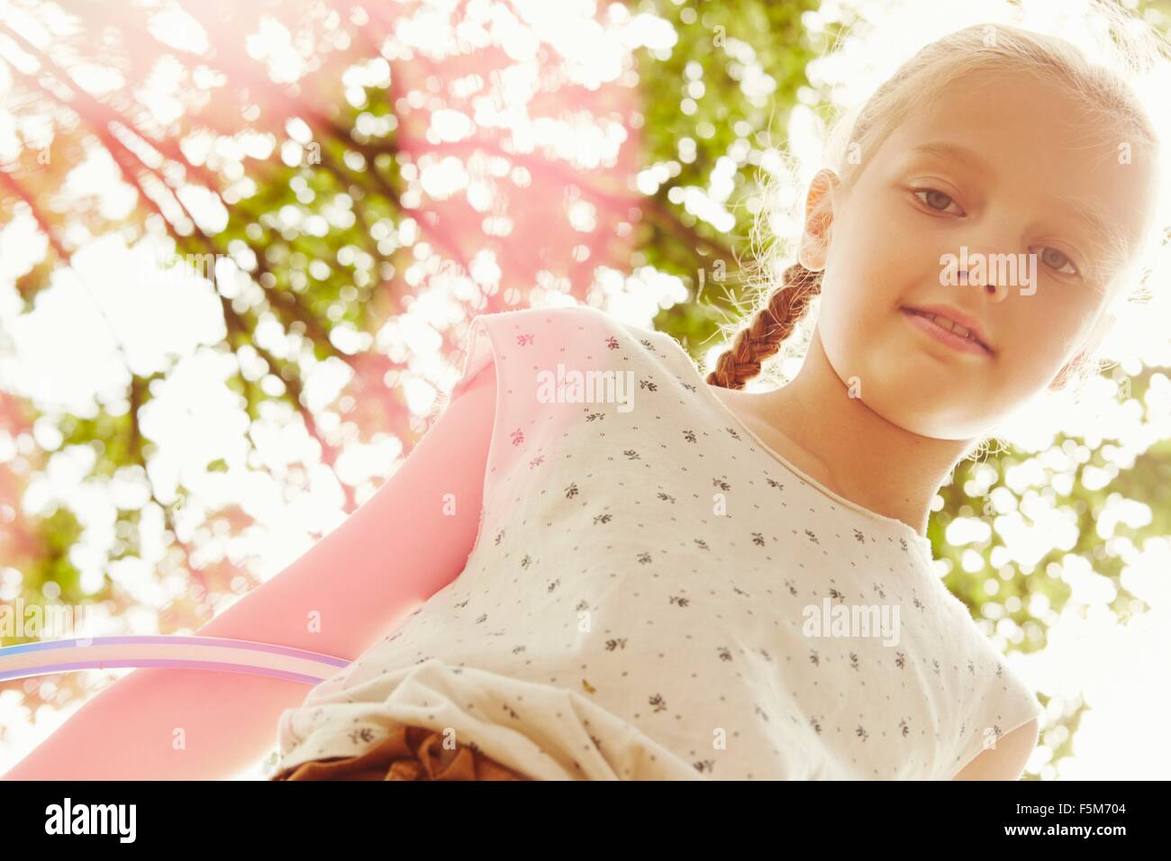 Low angle view of girl playing with hula hoop looking at camera smiling ...