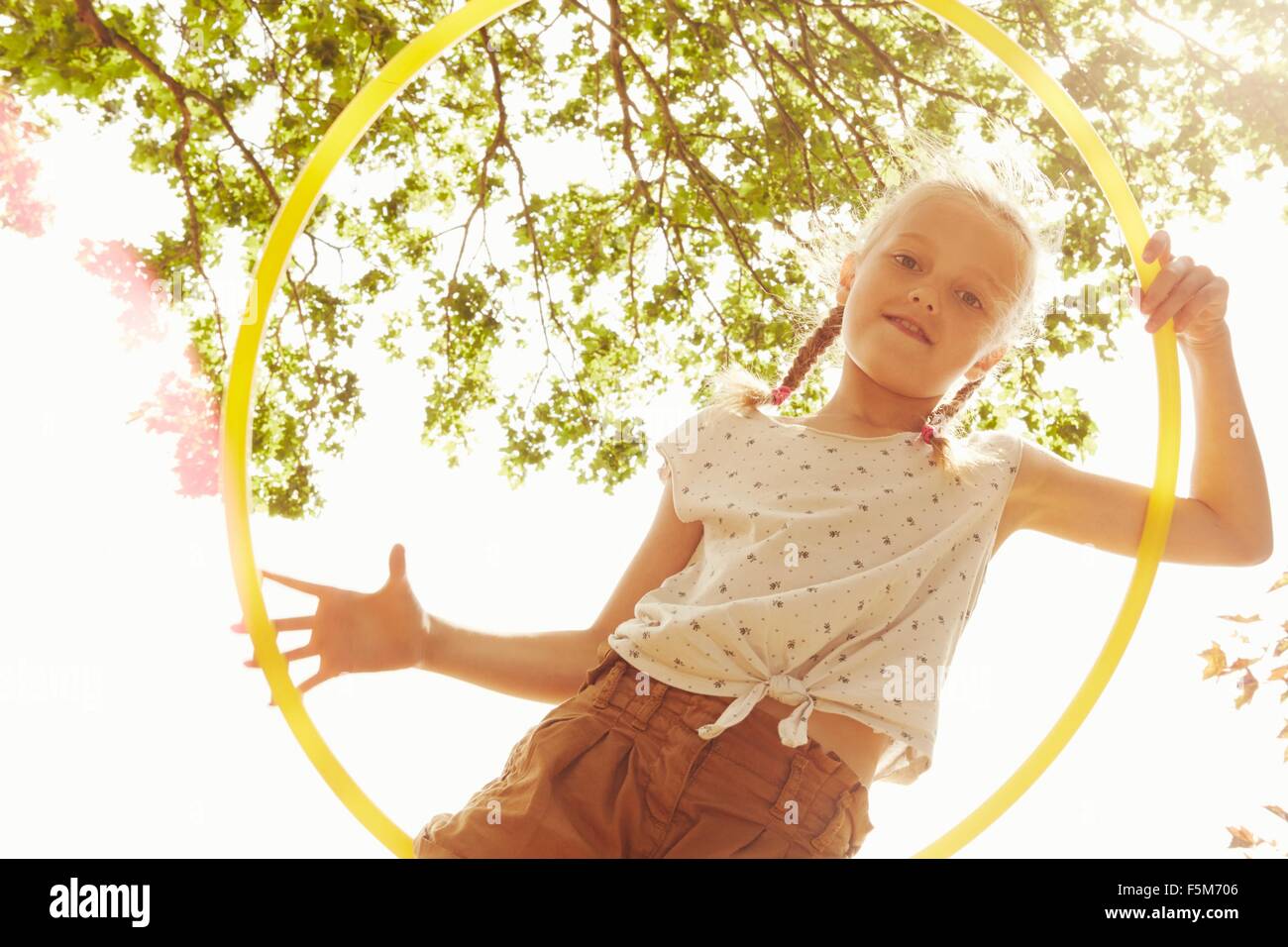 Low angle view of girl looking through hula hoop at camera smiling ...