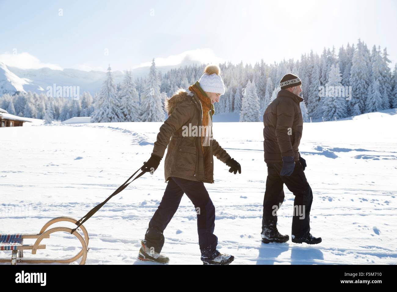 Side view of senior couple on snowy landscape pulling sledge ...