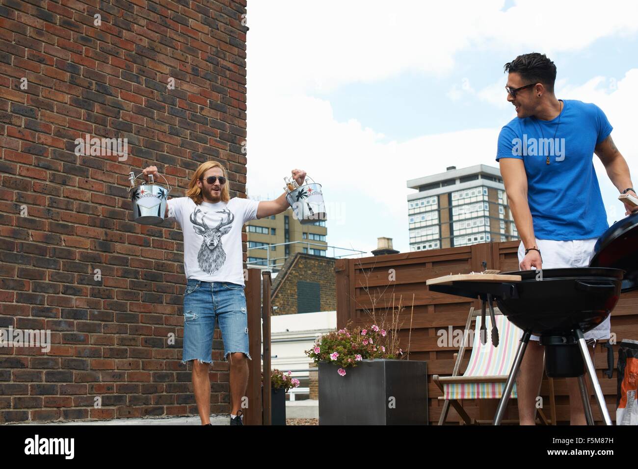 Young man carrying ice buckets at rooftop barbecue Stock Photo - Alamy