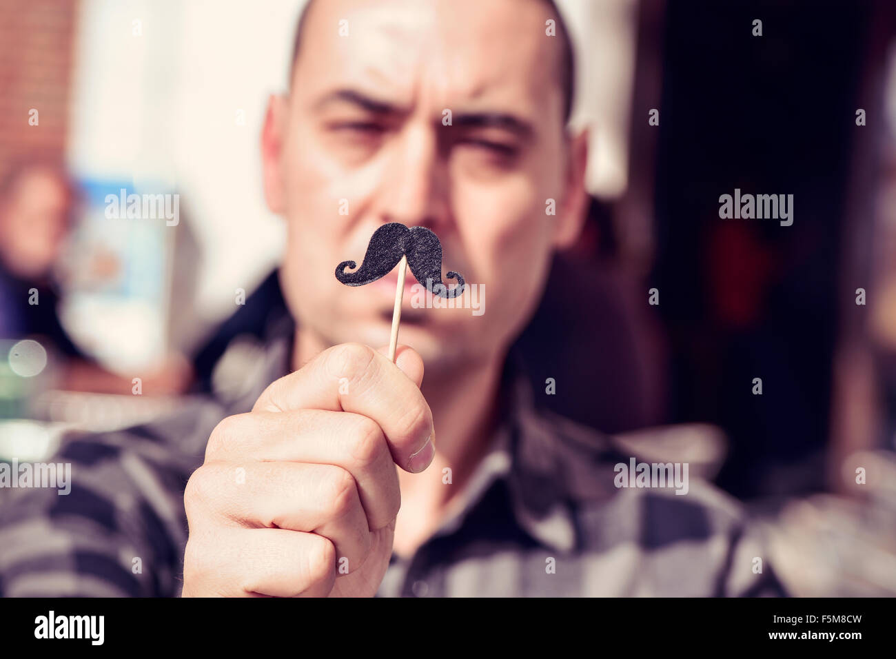 a young caucasian man holding a fake moustache in a stick in front of ...