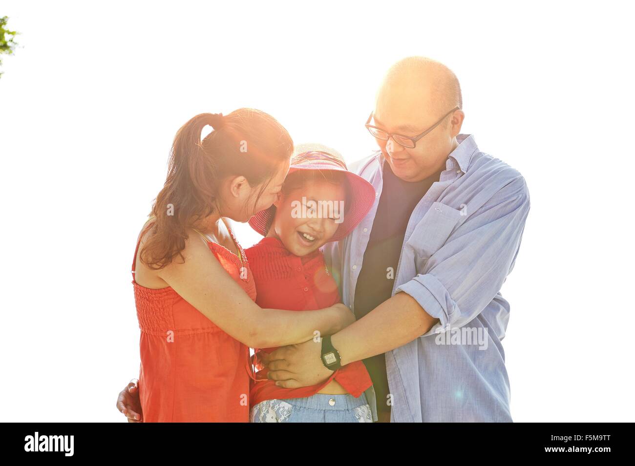 Parents hugging daughter in sunlight Stock Photo - Alamy