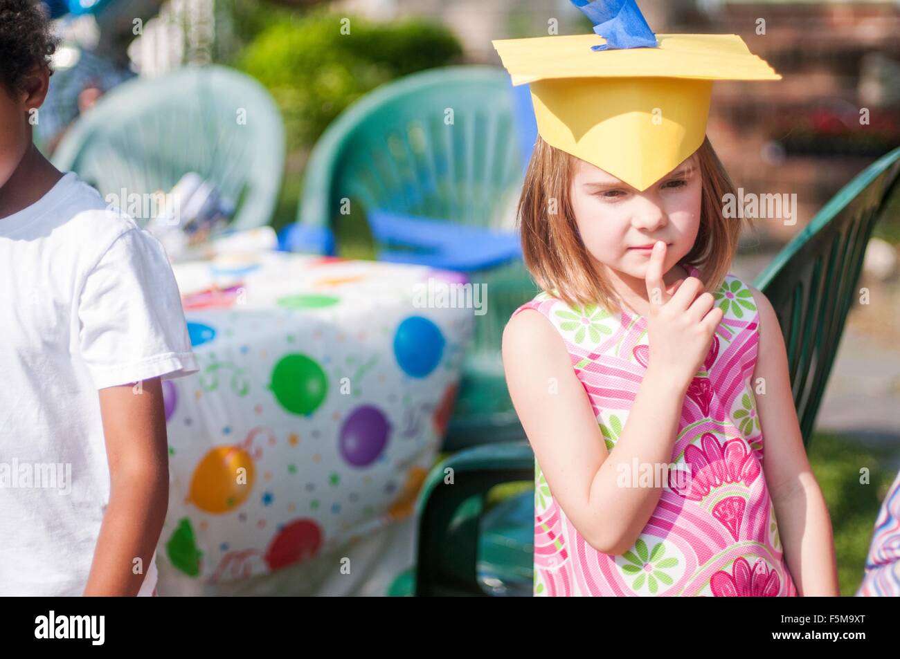 Portrait of young girl at kindergarten graduation, wearing paper mortar ...