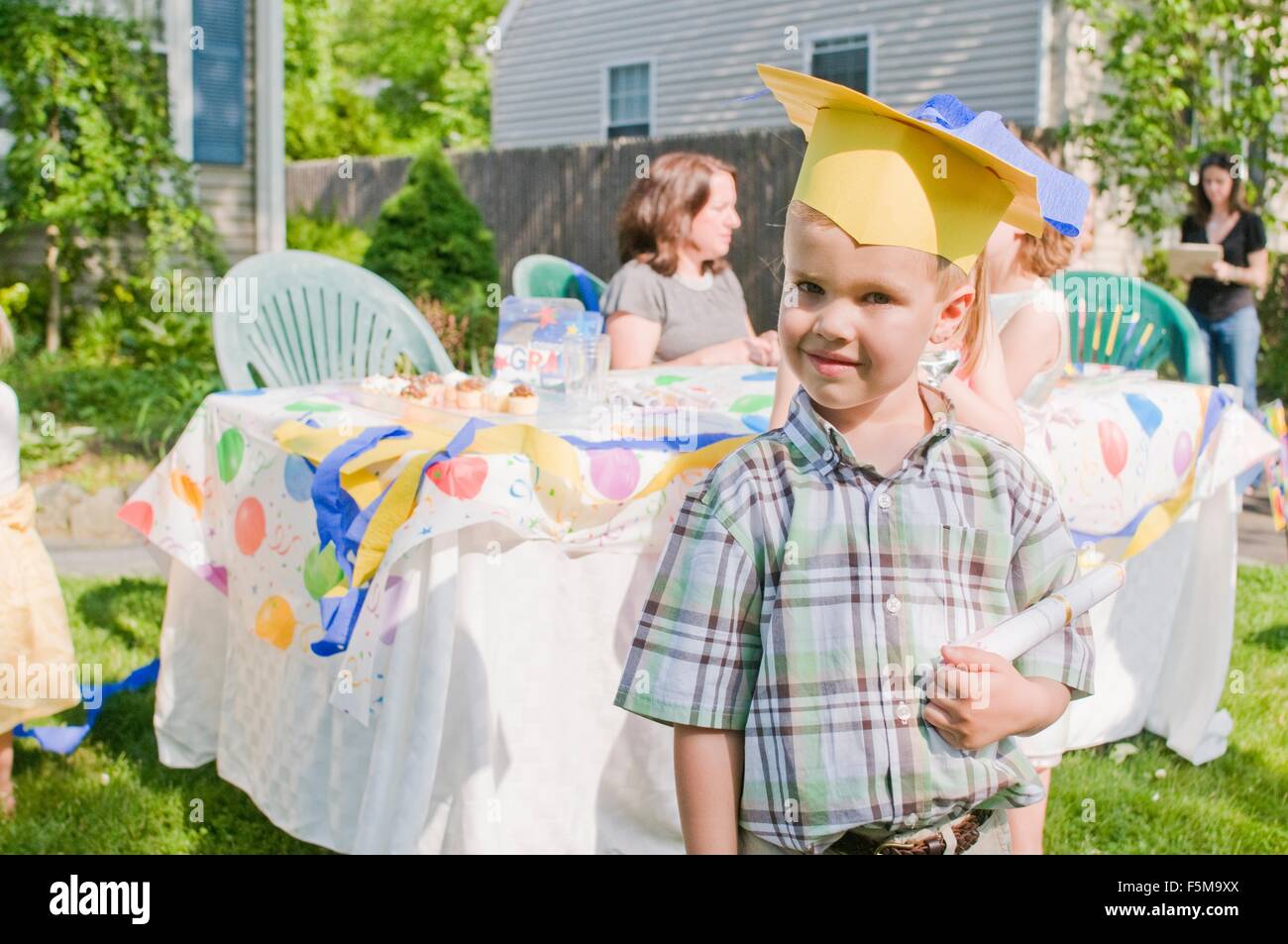 Portrait of young boy at kindergarten graduation, wearing paper mortar ...