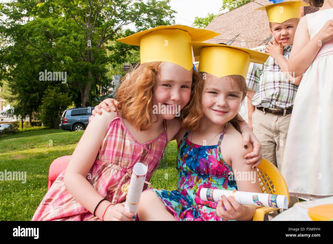 Two young girls at kindergarten graduation, wearing paper mortar boards ...