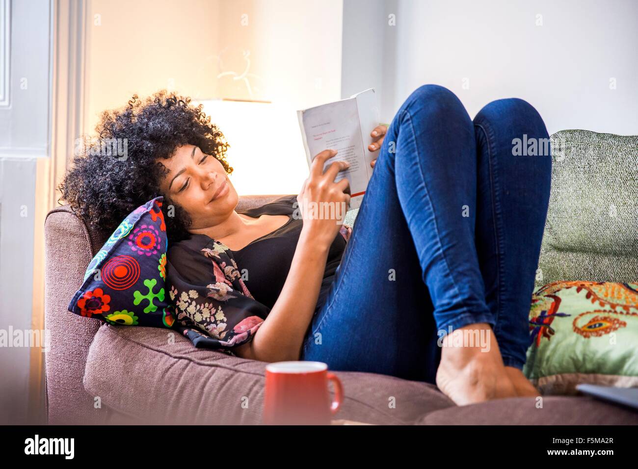 Mature woman reclining on sofa reading book Stock Photo - Alamy