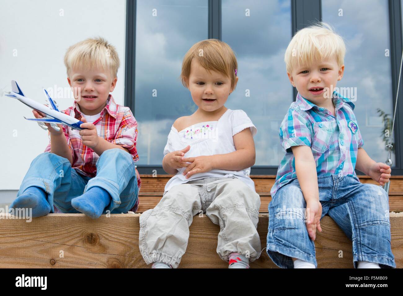 Boy with toy airplane and two toddlers sitting on patio Stock Photo - Alamy