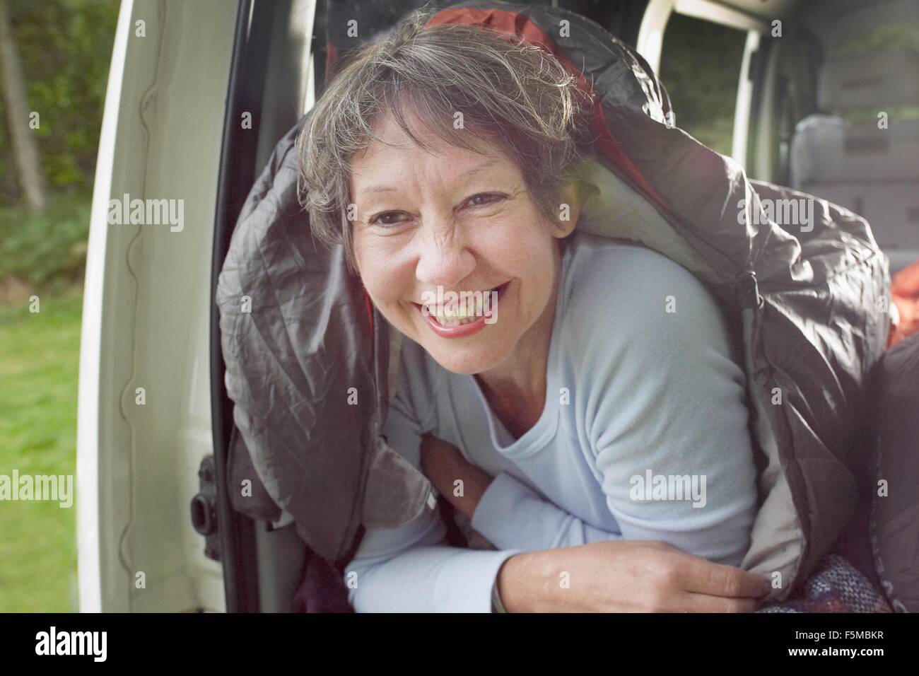 Portrait of senior woman inside sleeping bag, in open camper van Stock ...