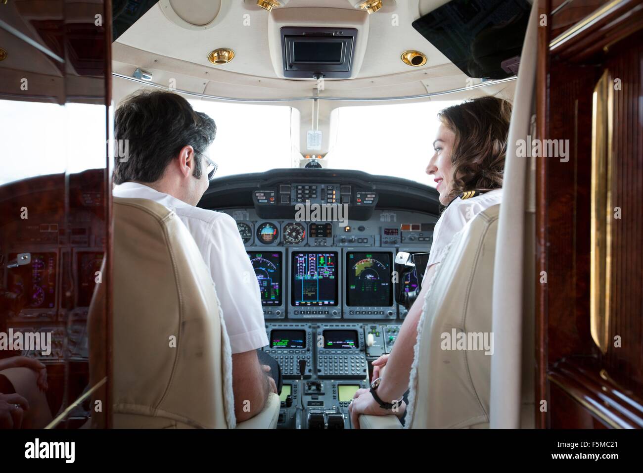 Rear view of male and female pilots talking in cockpit of private jet ...