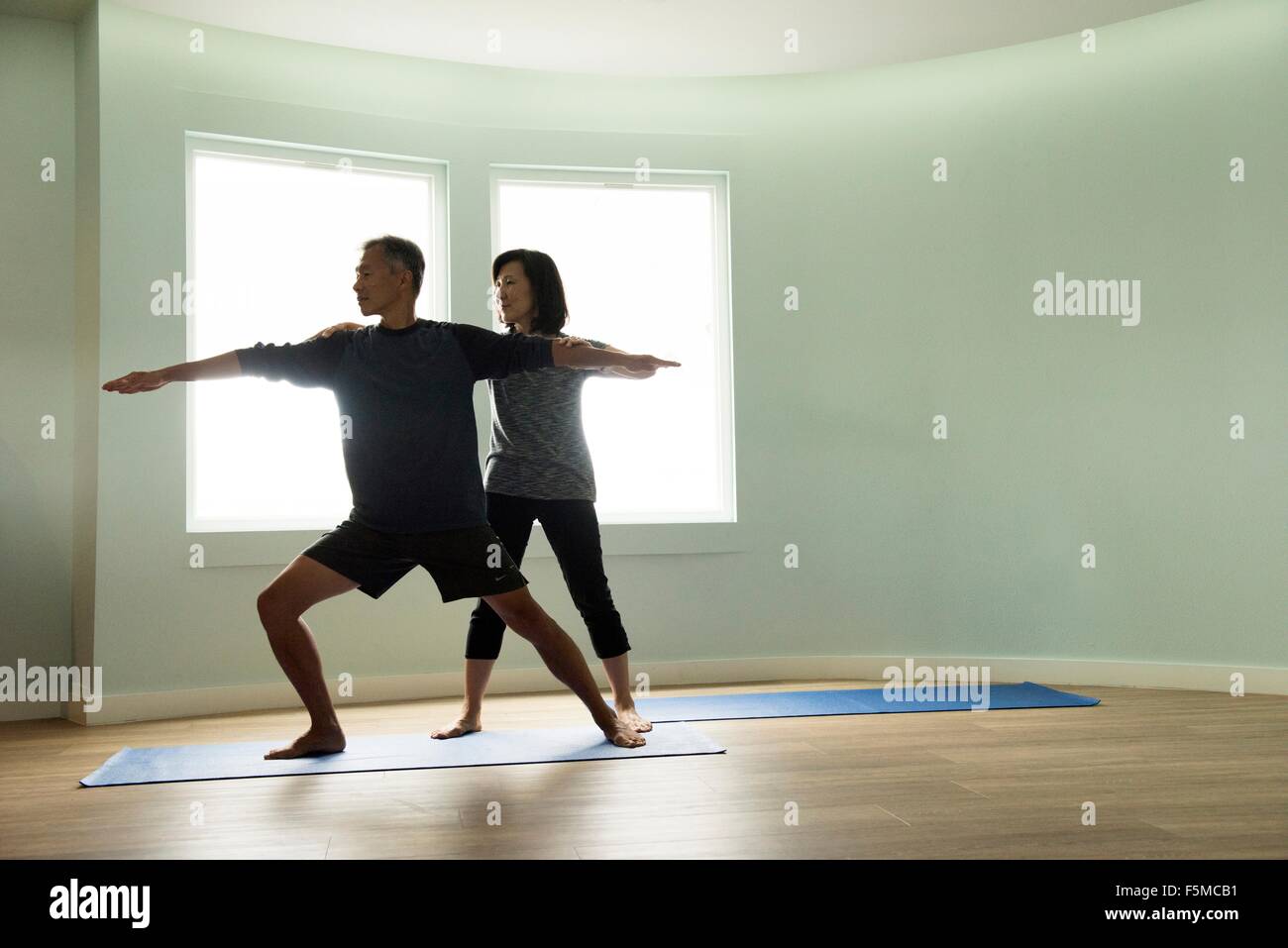 Front view of mature couple doing yoga together, correcting warrior ...