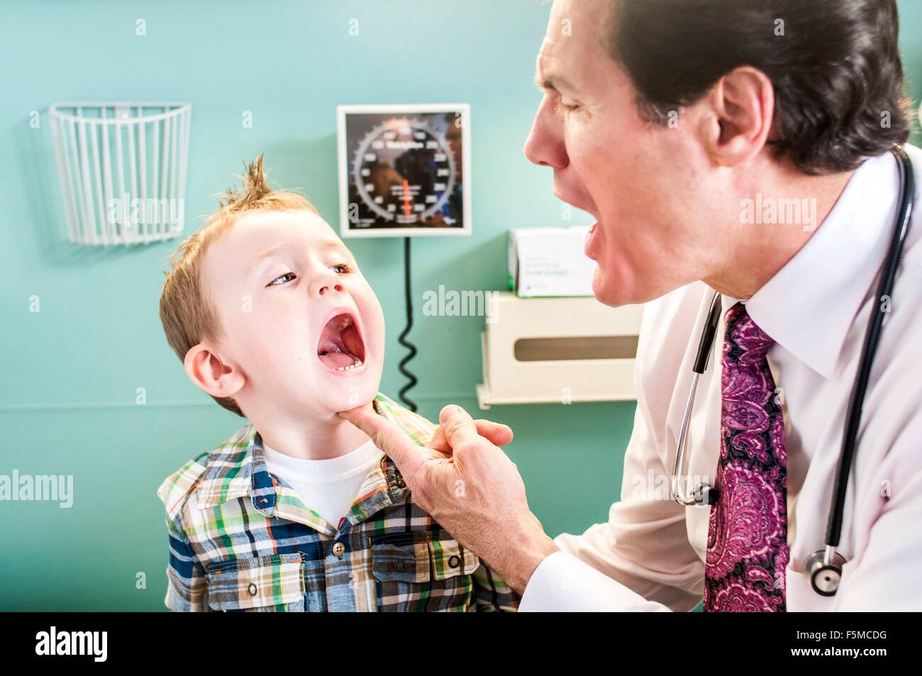 Young boy having check-up in doctor's office, doctor looking in boy's ...