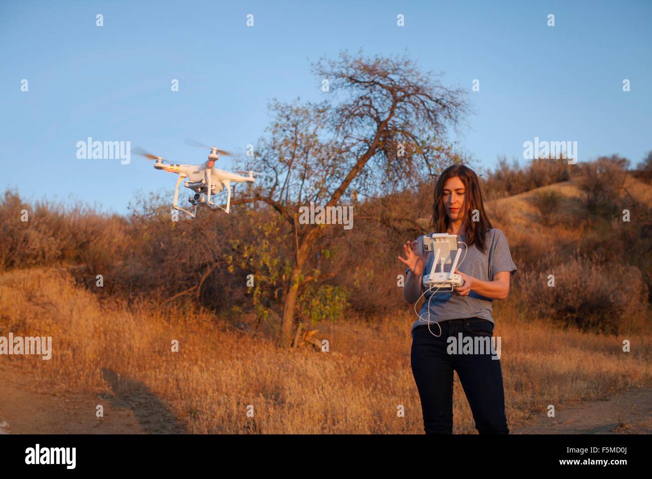 Female commercial operator on scrubland flying drone, looking down ...