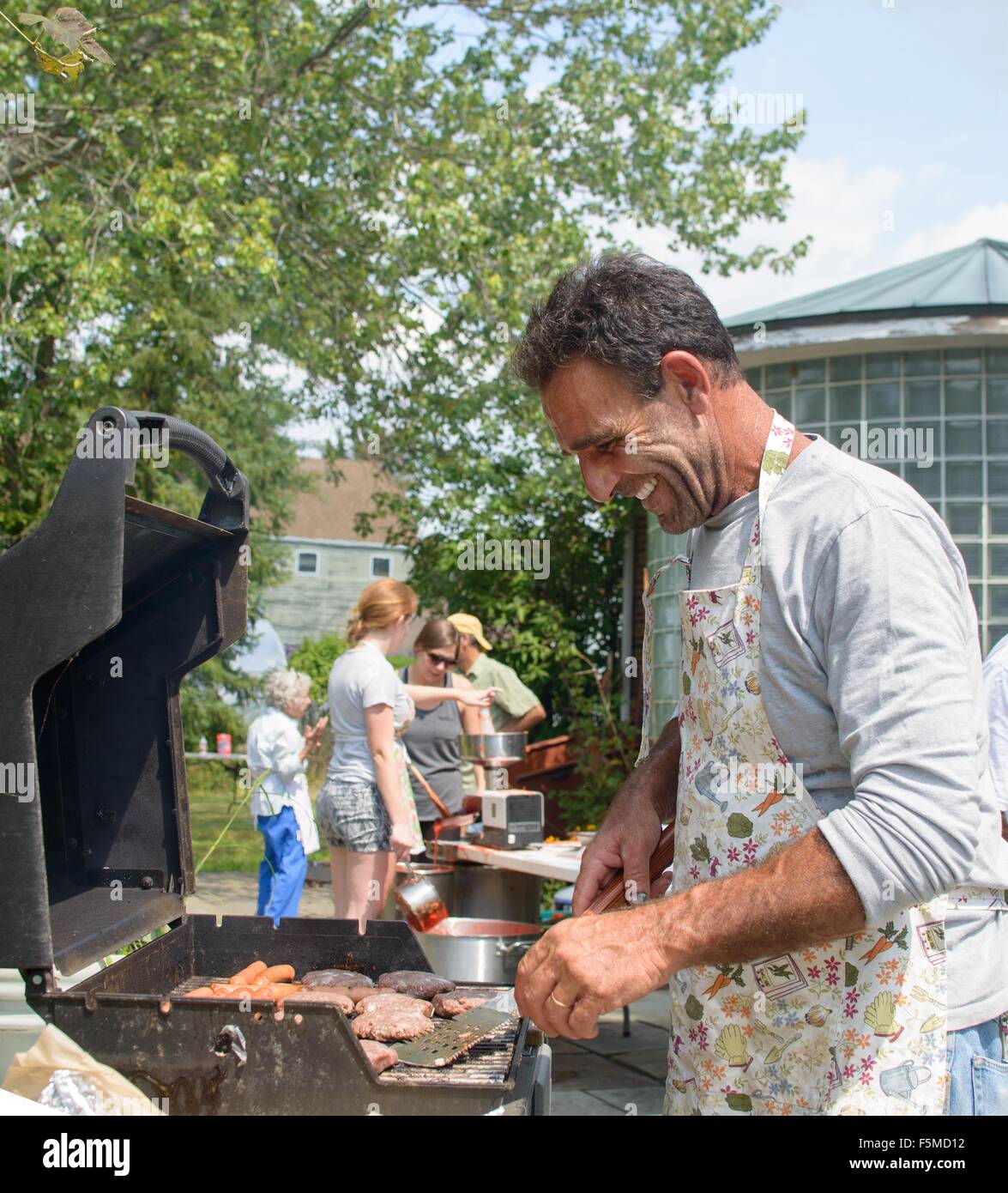 Side view of mature man cooking for family on barbecue looking down ...