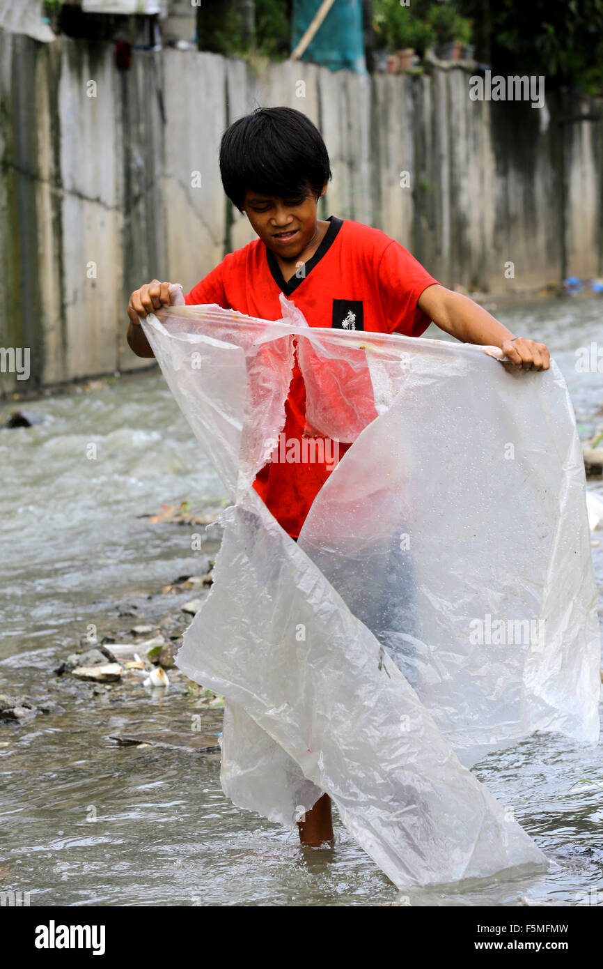 A boy washes plastic sheets in a stream to supply them to recycling ...